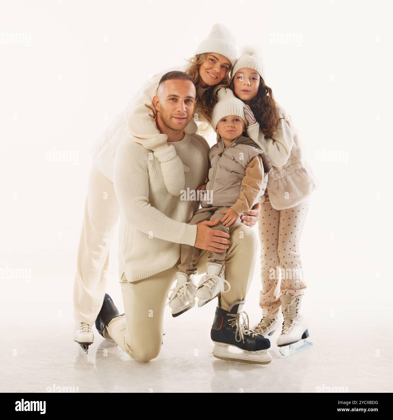 Whole family, bundled up in warm beige outfits, poses together for cozy moment on ice rink ...