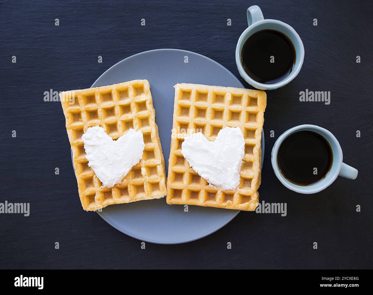 Delicious Belgian waffles with cream on a black background and two cups ...