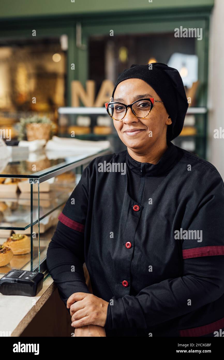 Confident female pastry chef in a modern bakery poses with an array of ...