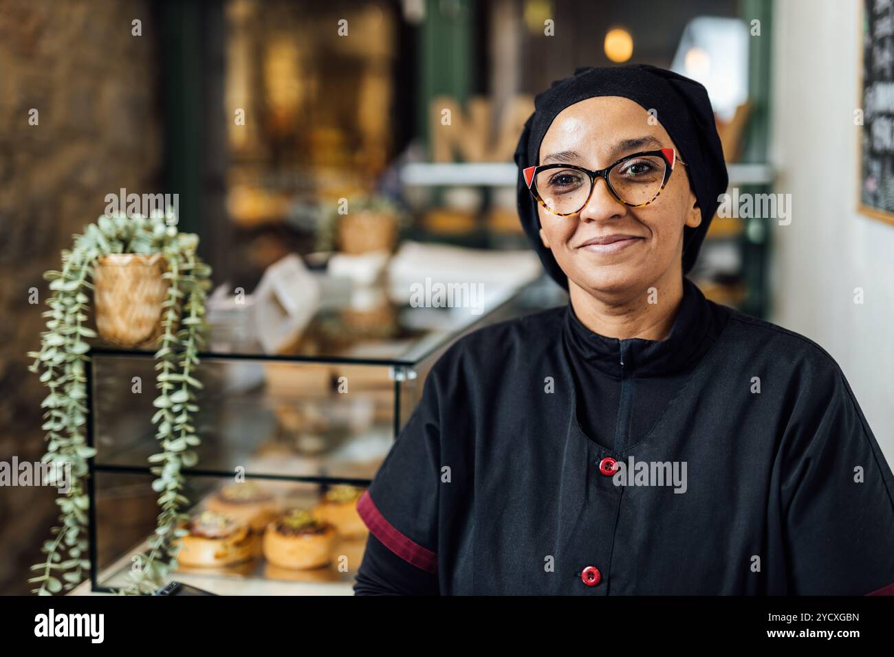 A smiling baker stands confidently by the counter in a cozy vegan bakery, showcasing a display ...