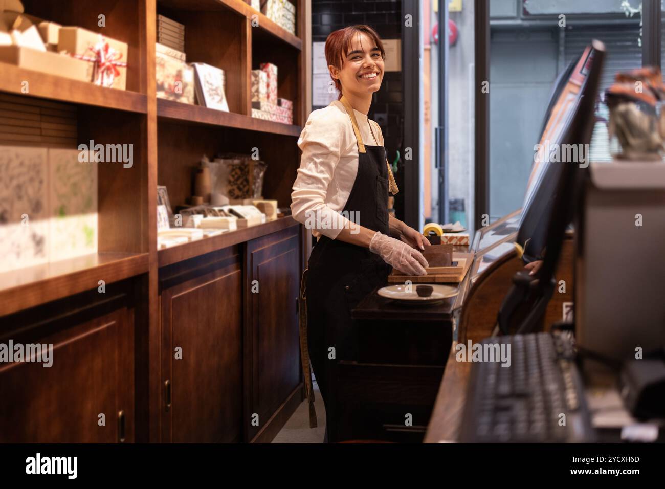 Shop assistant smiles as she works in a chocolate store, wearing gloves ...