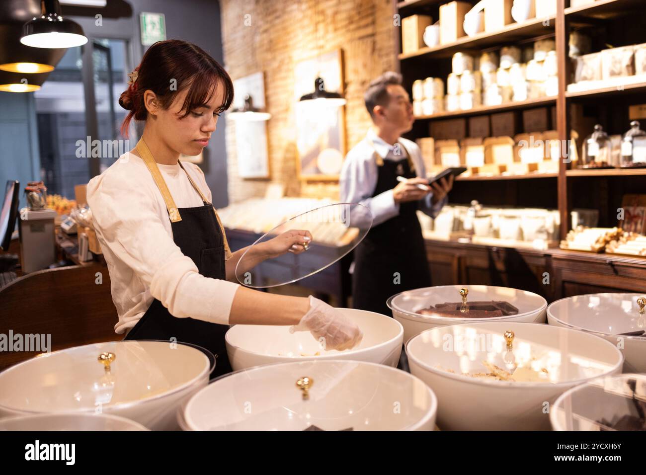 A concentrated young woman placing chocolates in large white bowls in a ...