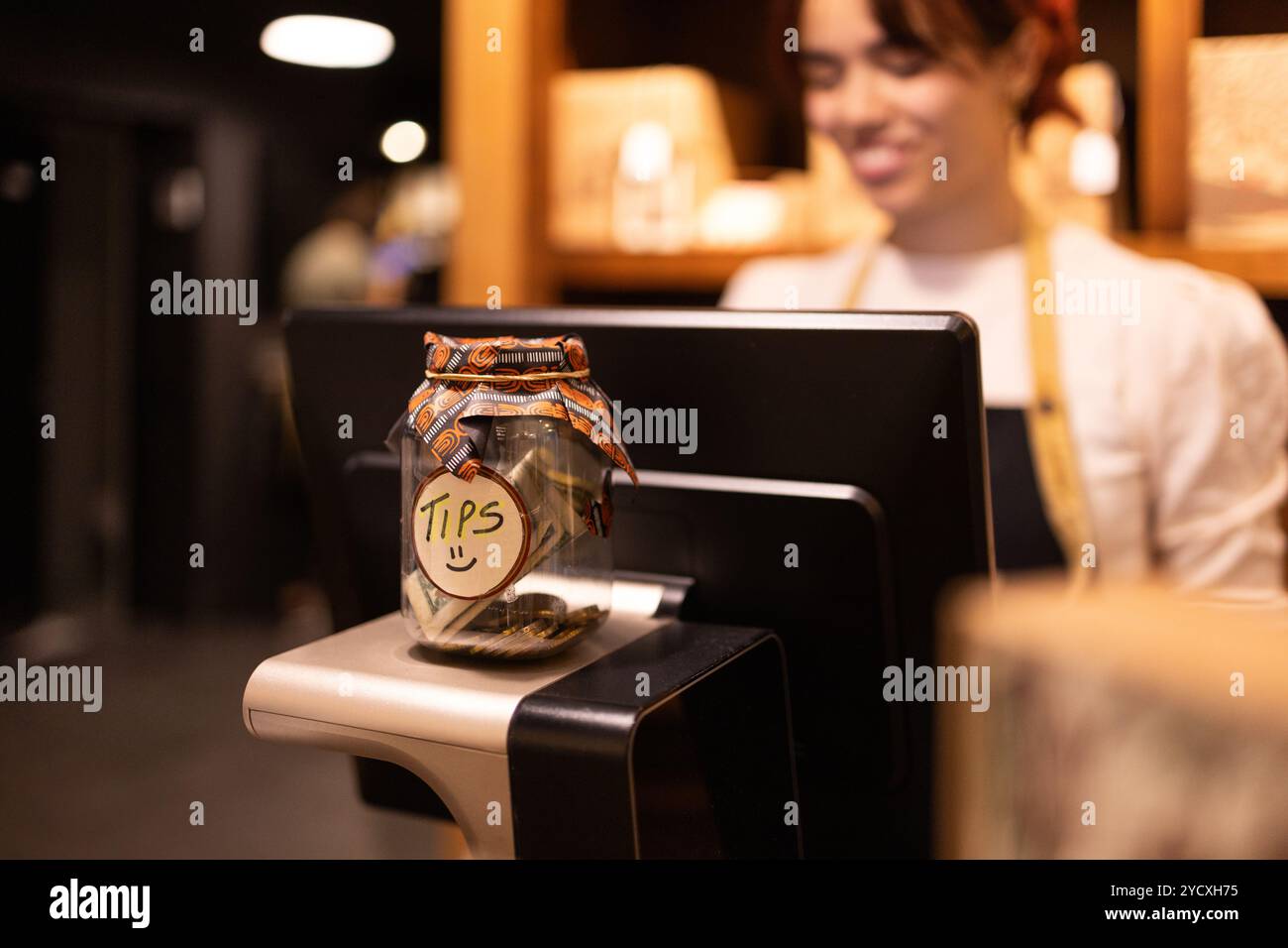 A smiling female cashier behind a computer screen with a tip jar in the ...