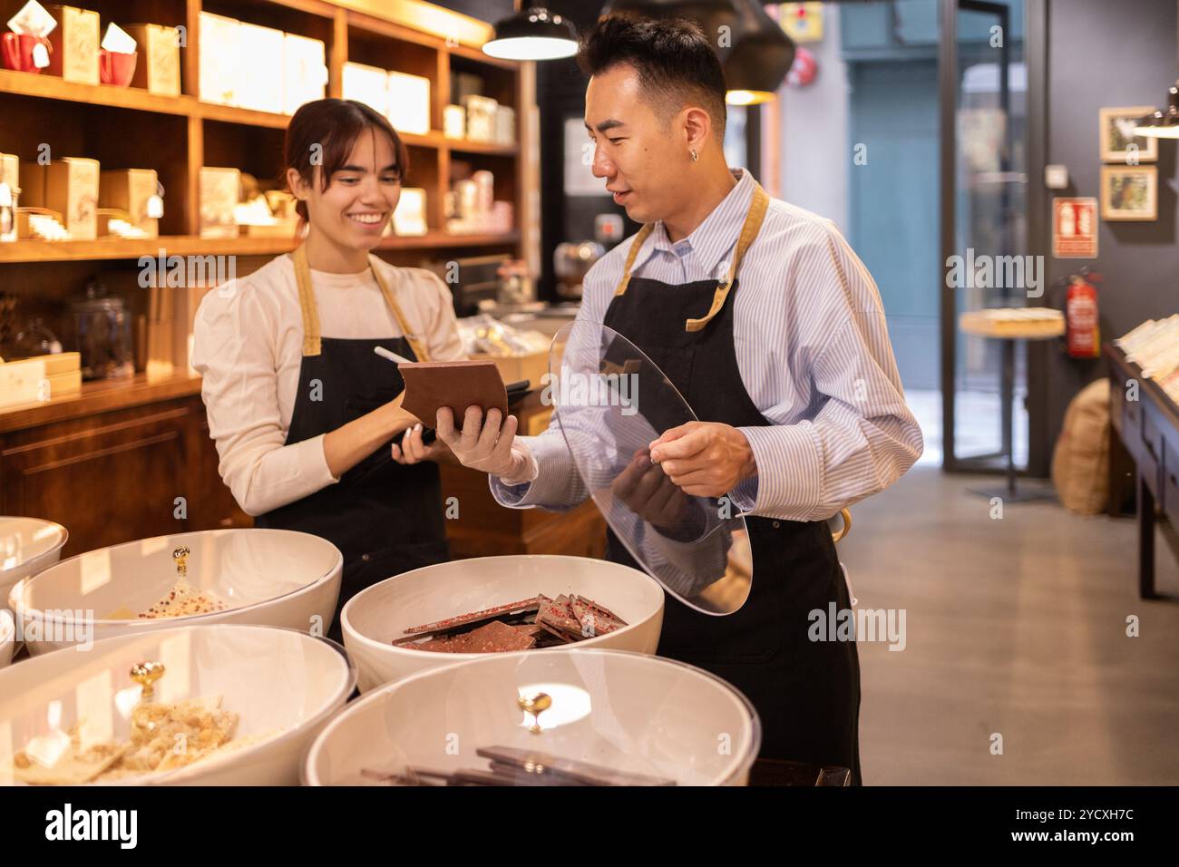 Two smiling workers in a chocolate shop, with various types of ...
