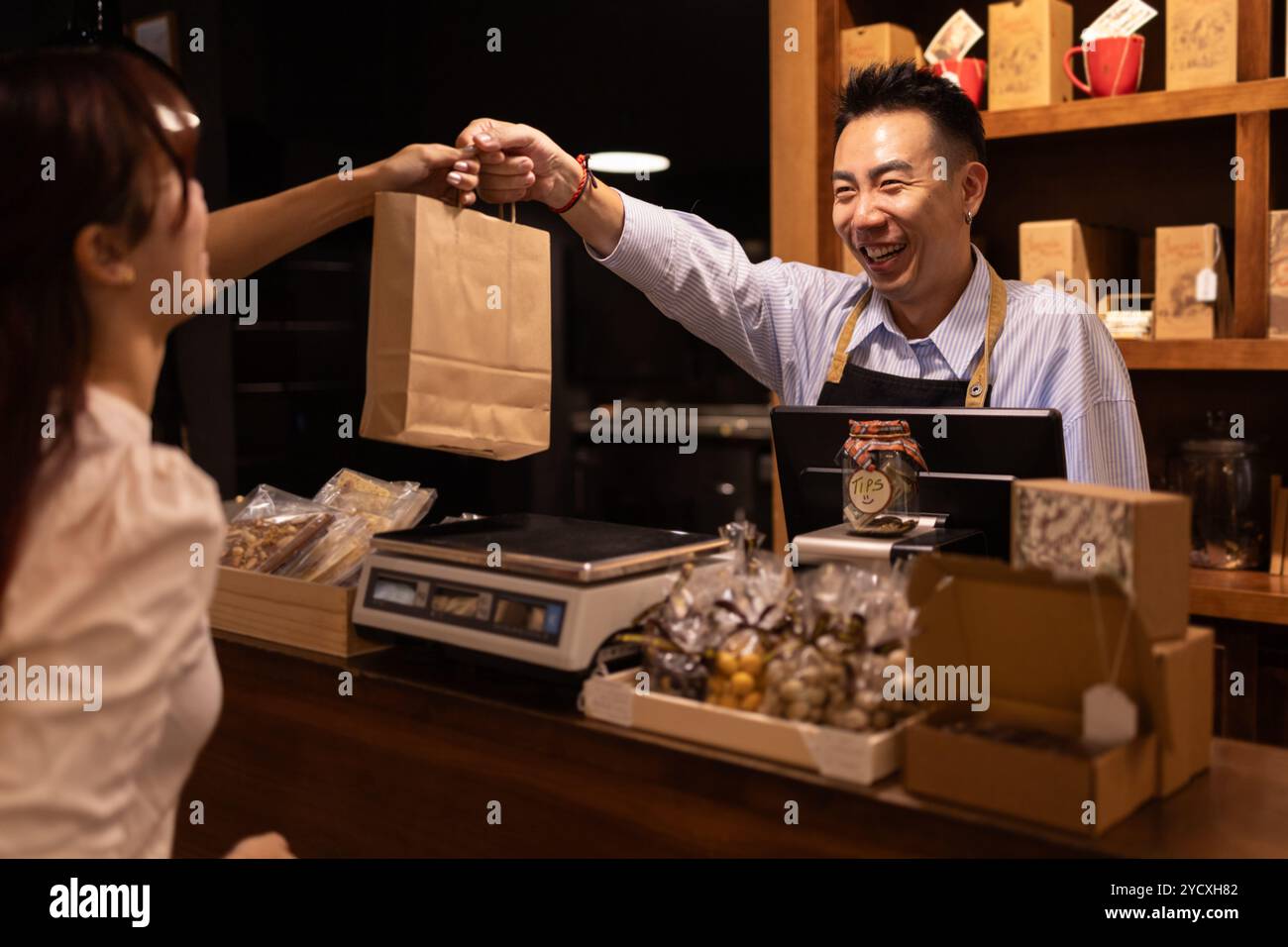 The cheerful clerk of a chocolate shop hands a bag with purchased ...
