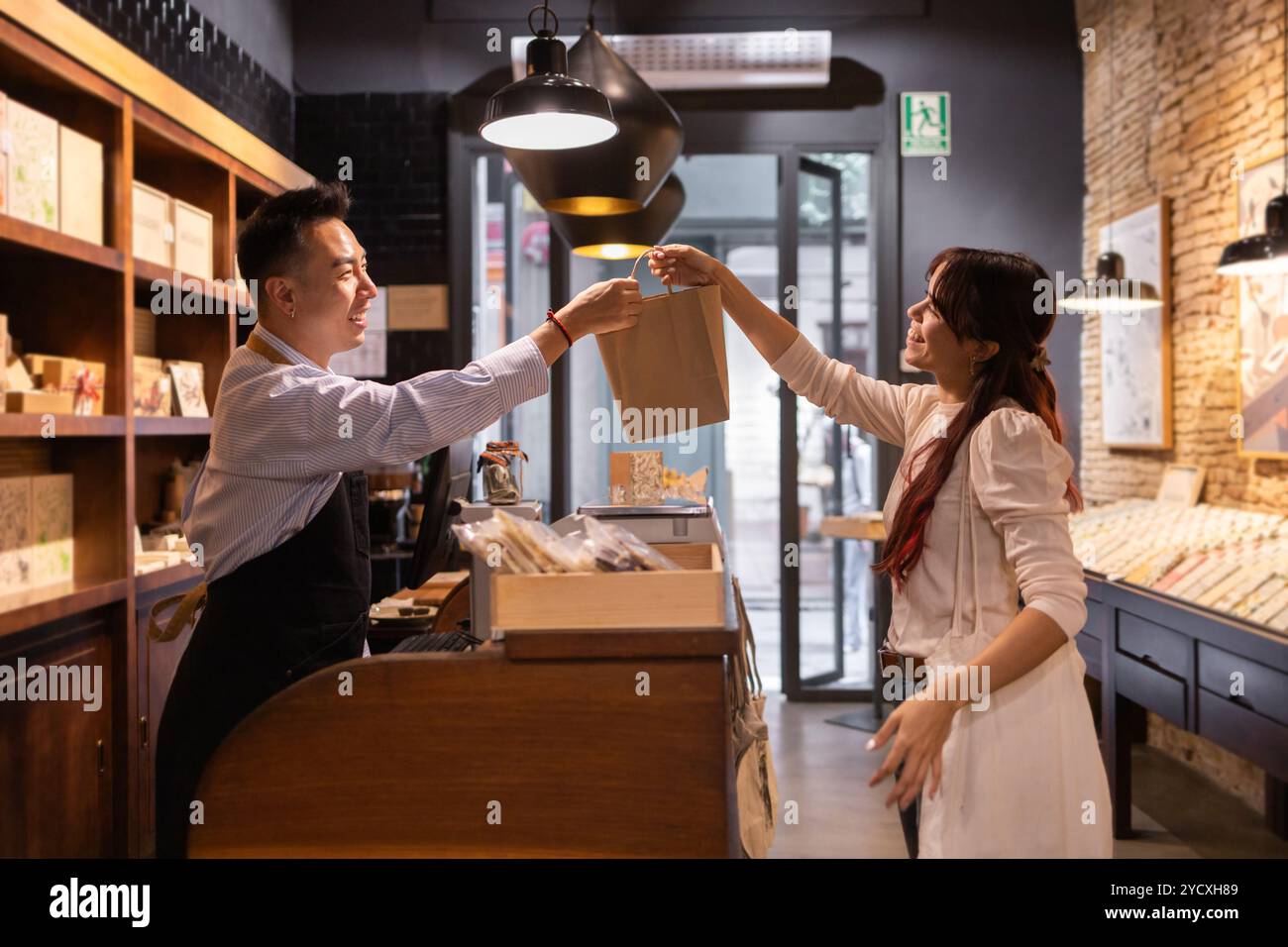 An asian man hands a paper bag to a smiling woman in a quaint chocolate ...