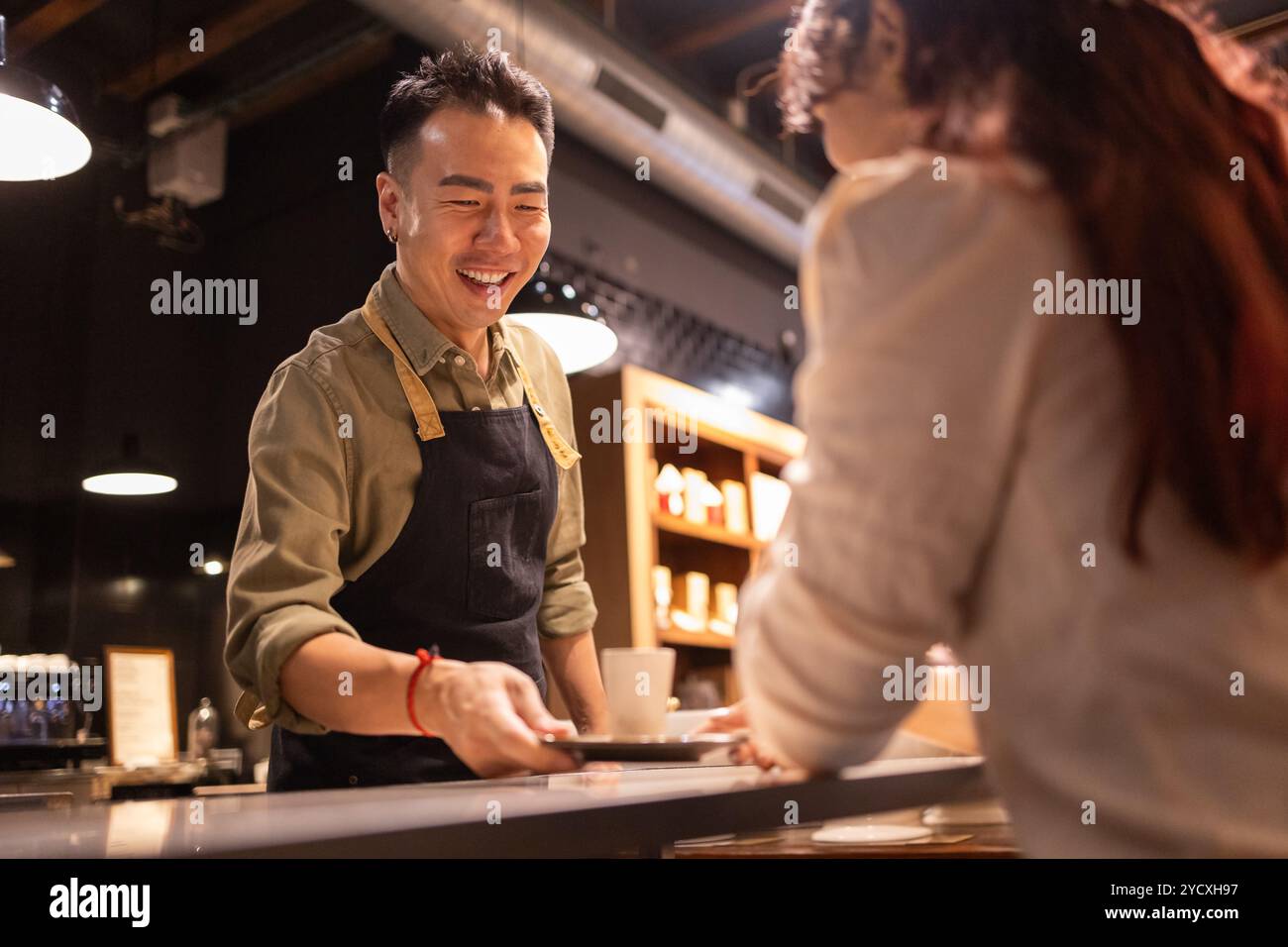 A cheerful asian male chocolatier in an apron interacts with a customer ...