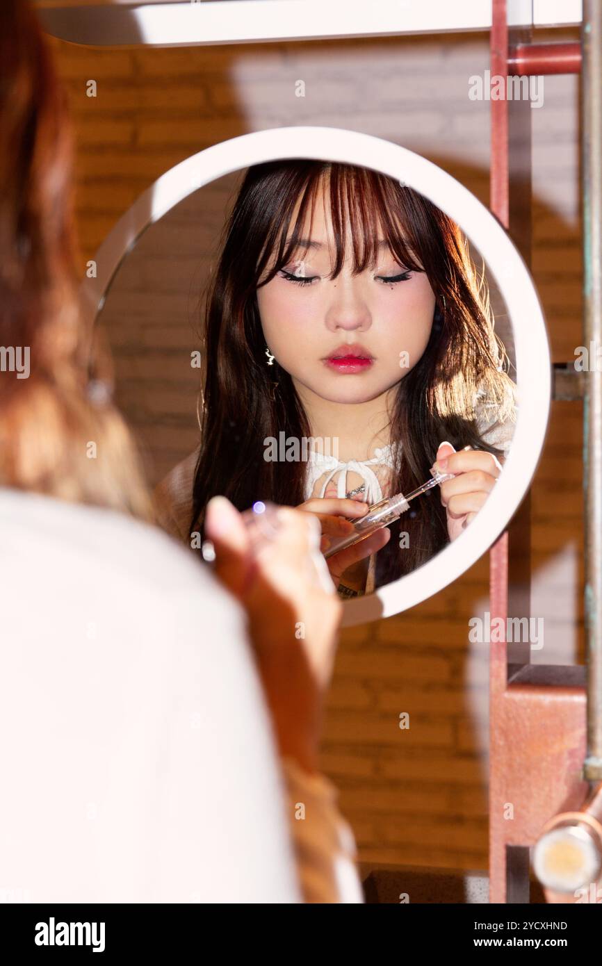 A young Chinese Gen Z girl focused on applying makeup, gracefully using ...