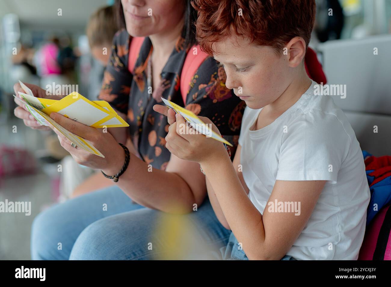 A young red haired boy and a cropped unrecognizable woman sit in an ...