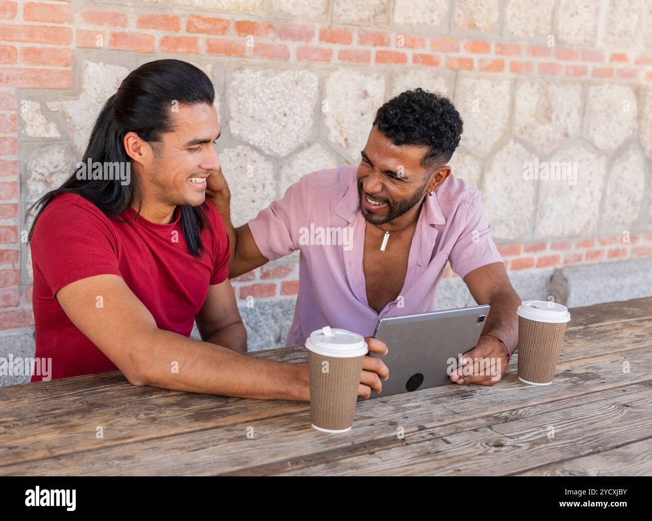 An affectionate moment between two gay men sitting at a city table ...