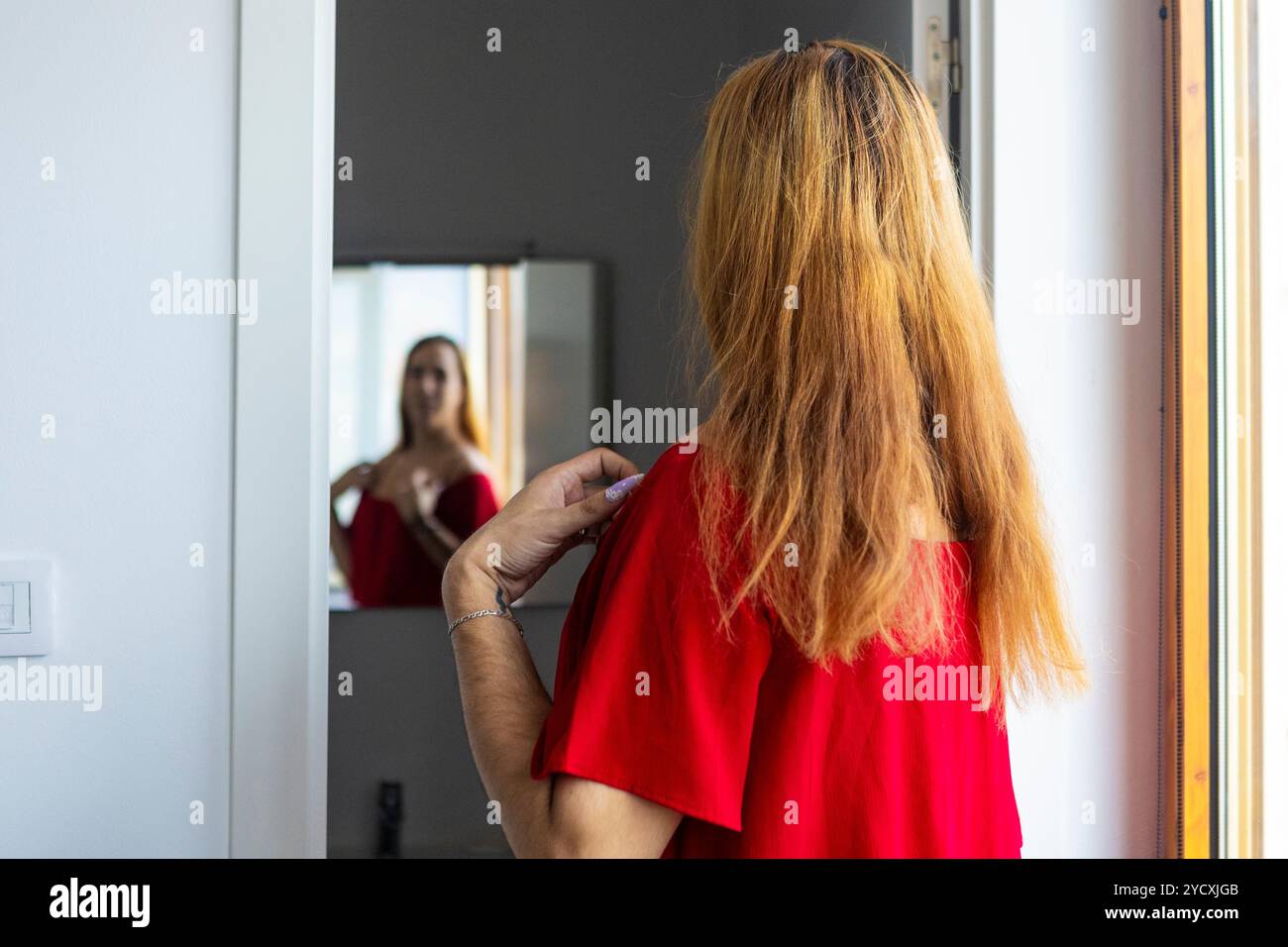 A trans woman, captured from behind, gazes into the mirror while ...