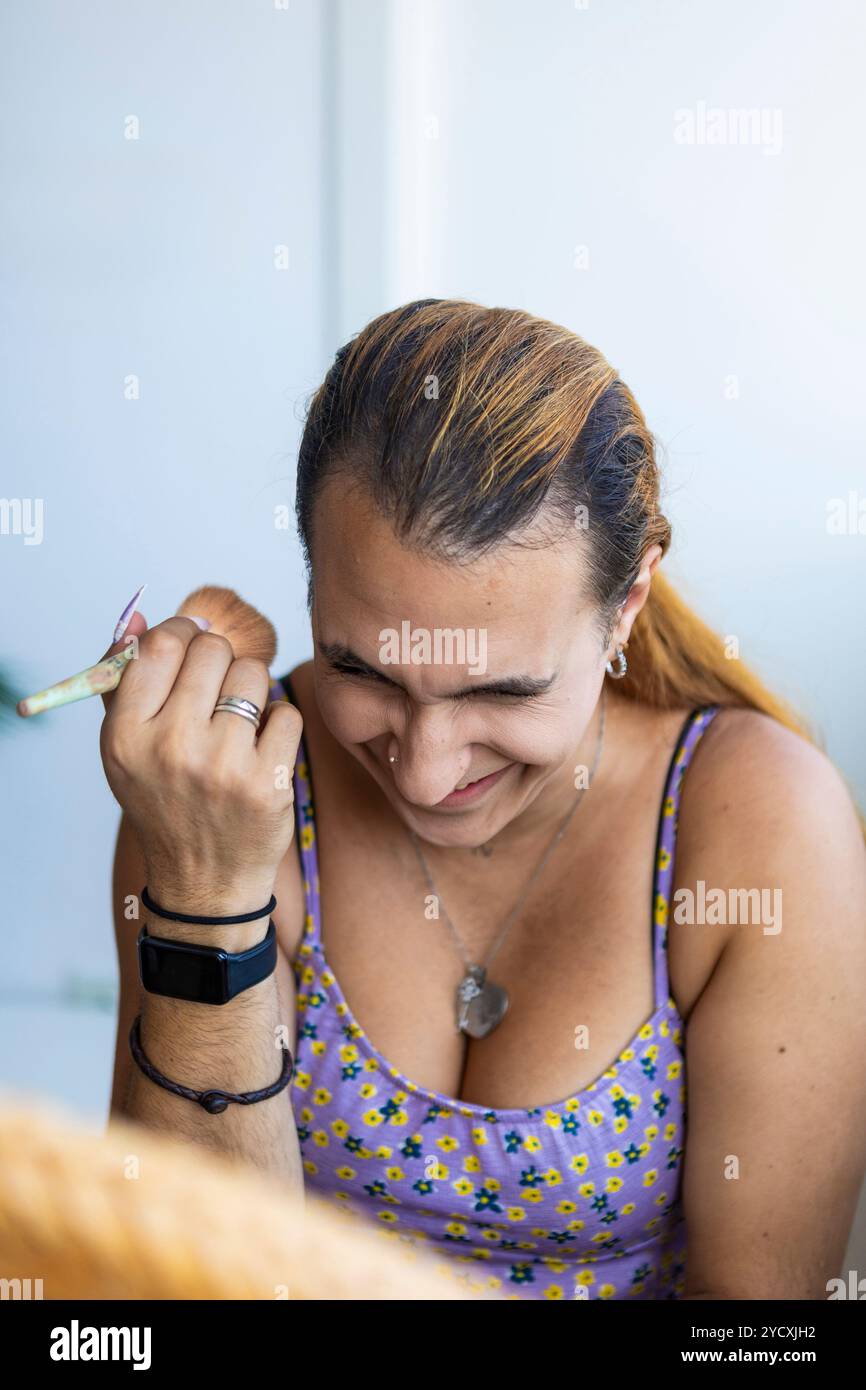 A smiling trans woman expertly applies makeup, evidencing her joyful morning ritual The image ...