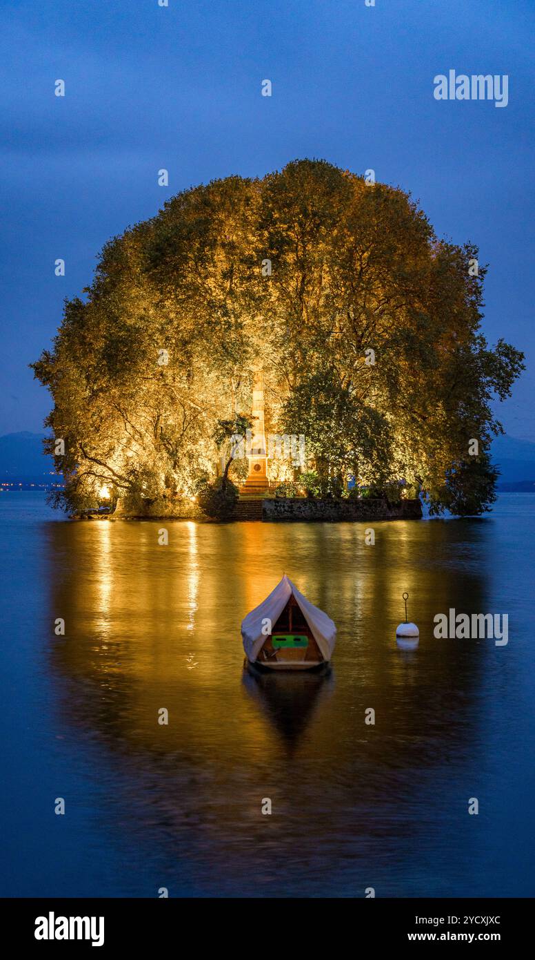 An illuminated tree and monument on Ile de la Harpe with a boat in the ...