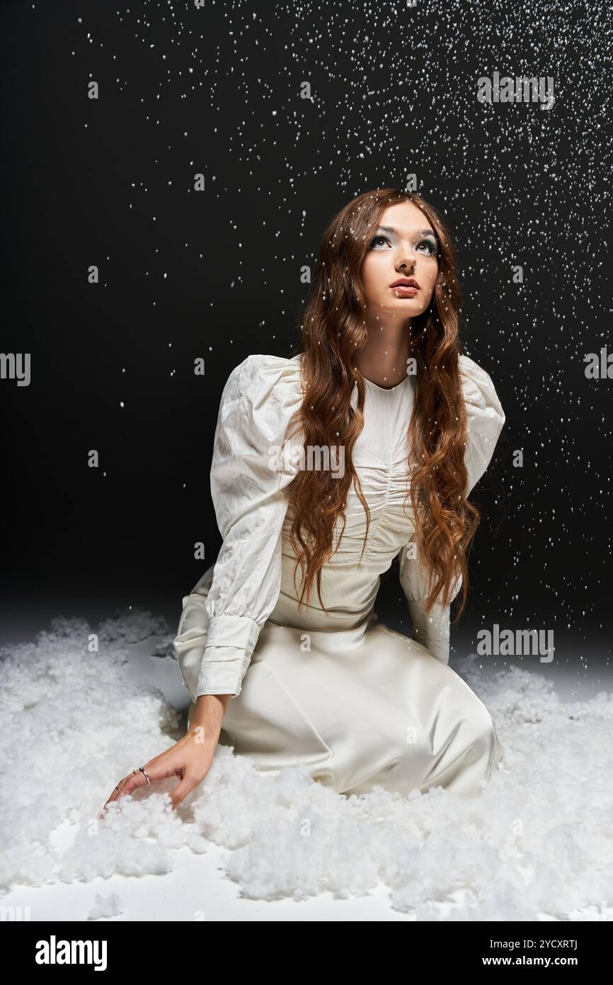 Snowflakes gently fall around a young woman in a striking white dress ...
