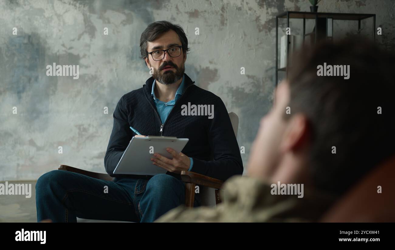 Worried mature Caucasian psychologist counselor writing notes listening ...