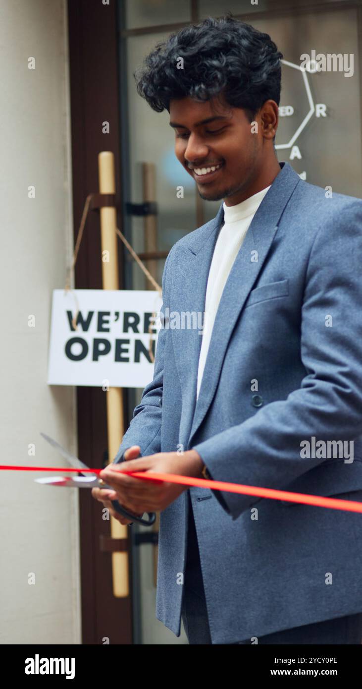 Business owner cutting red ribbon to symbolize the official opening of ...