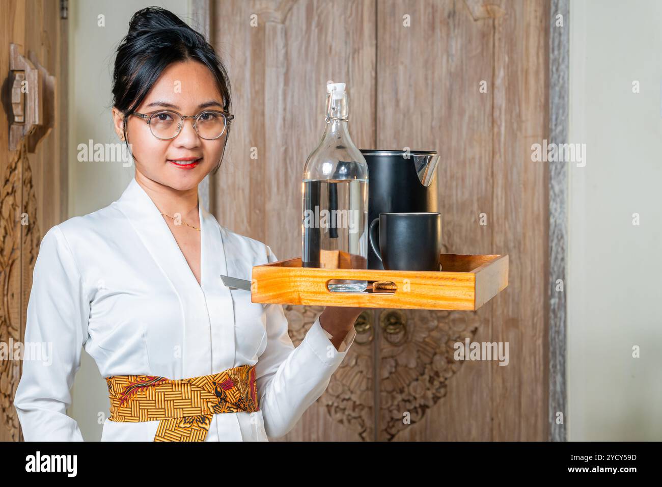 A hotel staff member in uniform holding a tray with a water bottle, cup ...