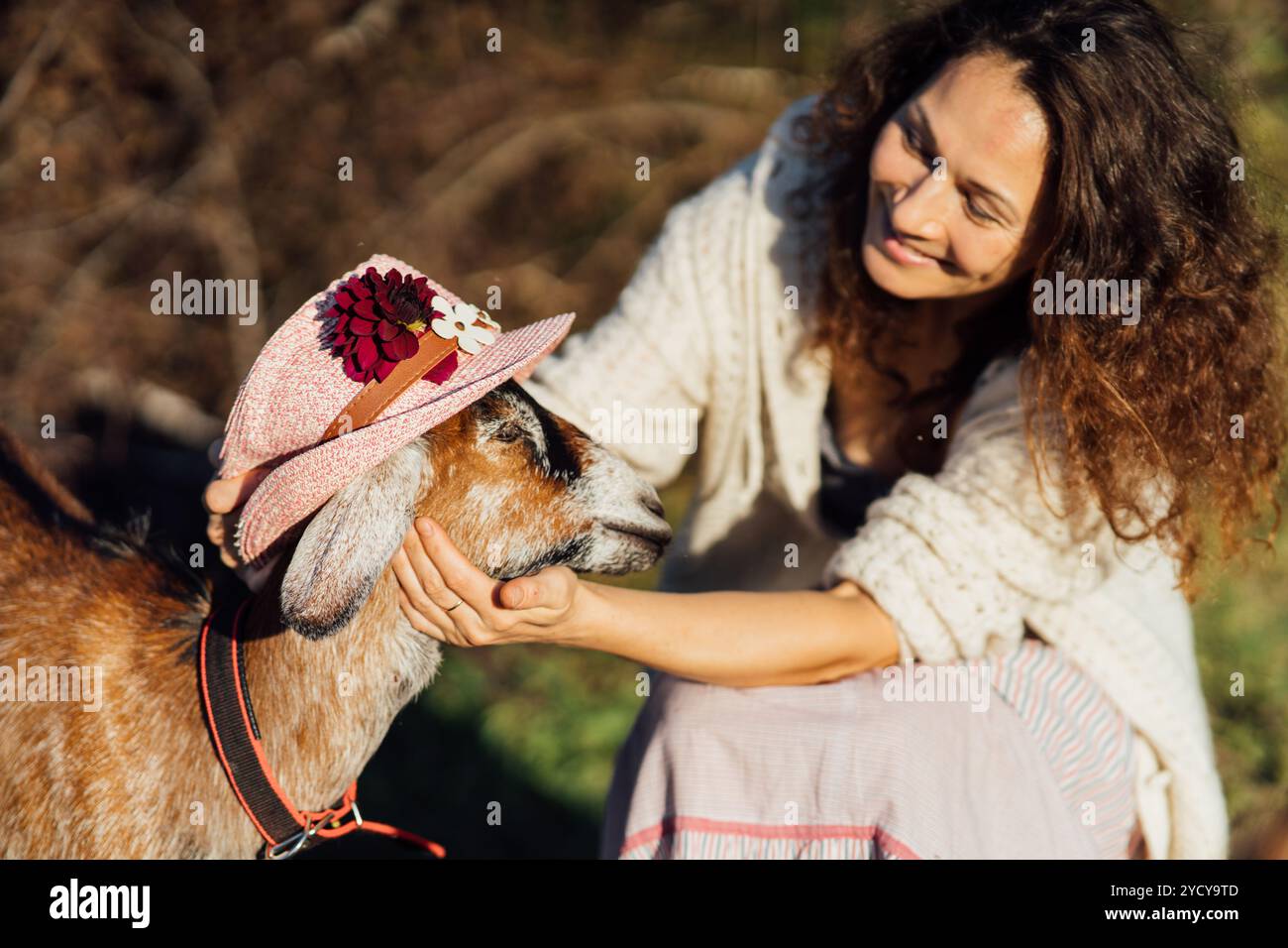 Woman in a hat and curly hair bonding with goats on a farm Stock Photo ...