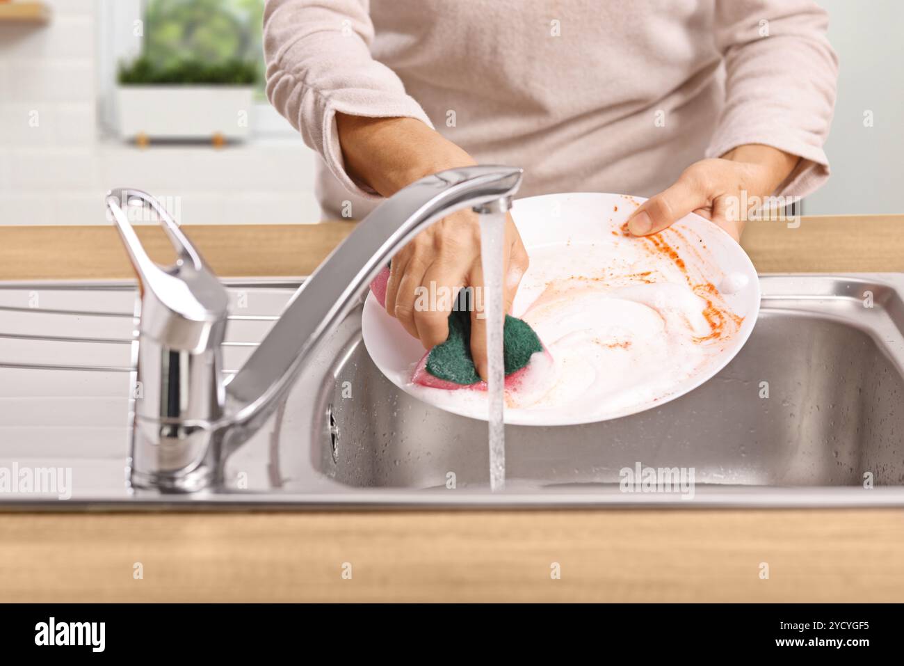 Woman washing a dirty plate with a sponge in a stainless steel sink in ...