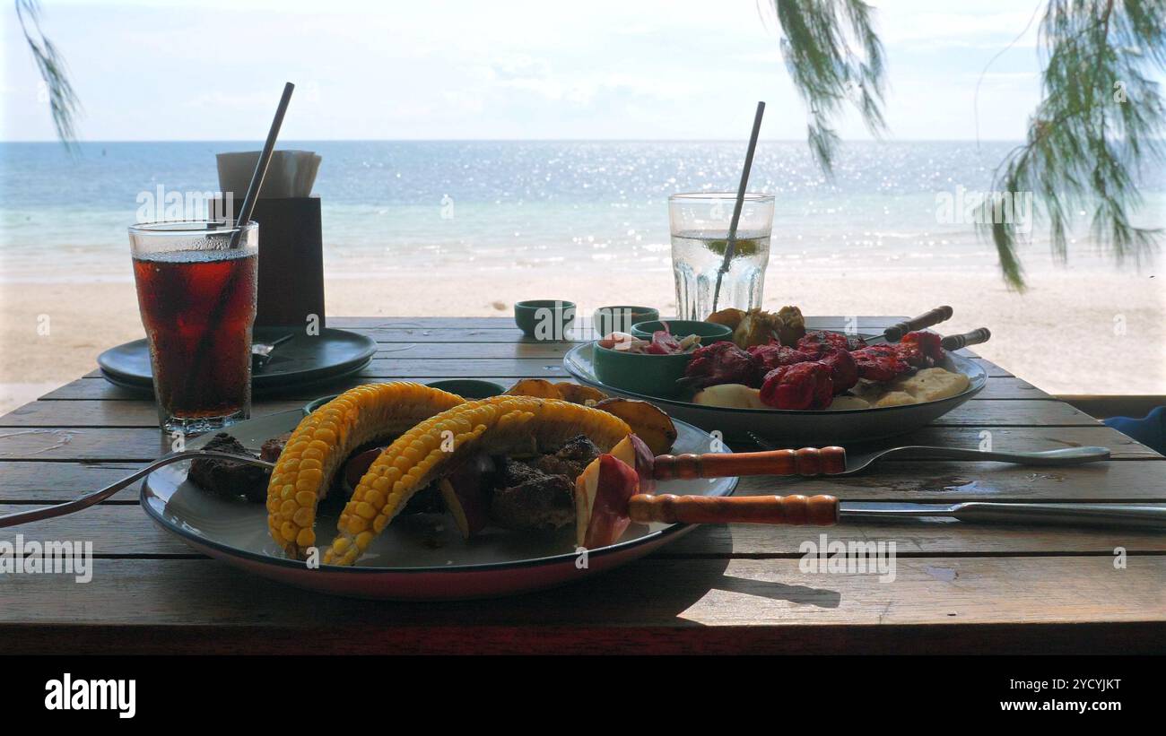 Delicious outdoor meal by beach with corn, skewers, and refreshing ...