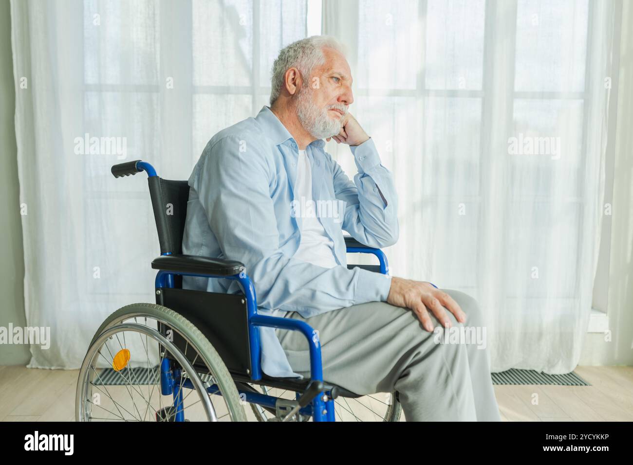 Sad senior man sitting in wheelchair looking out window in retirement ...