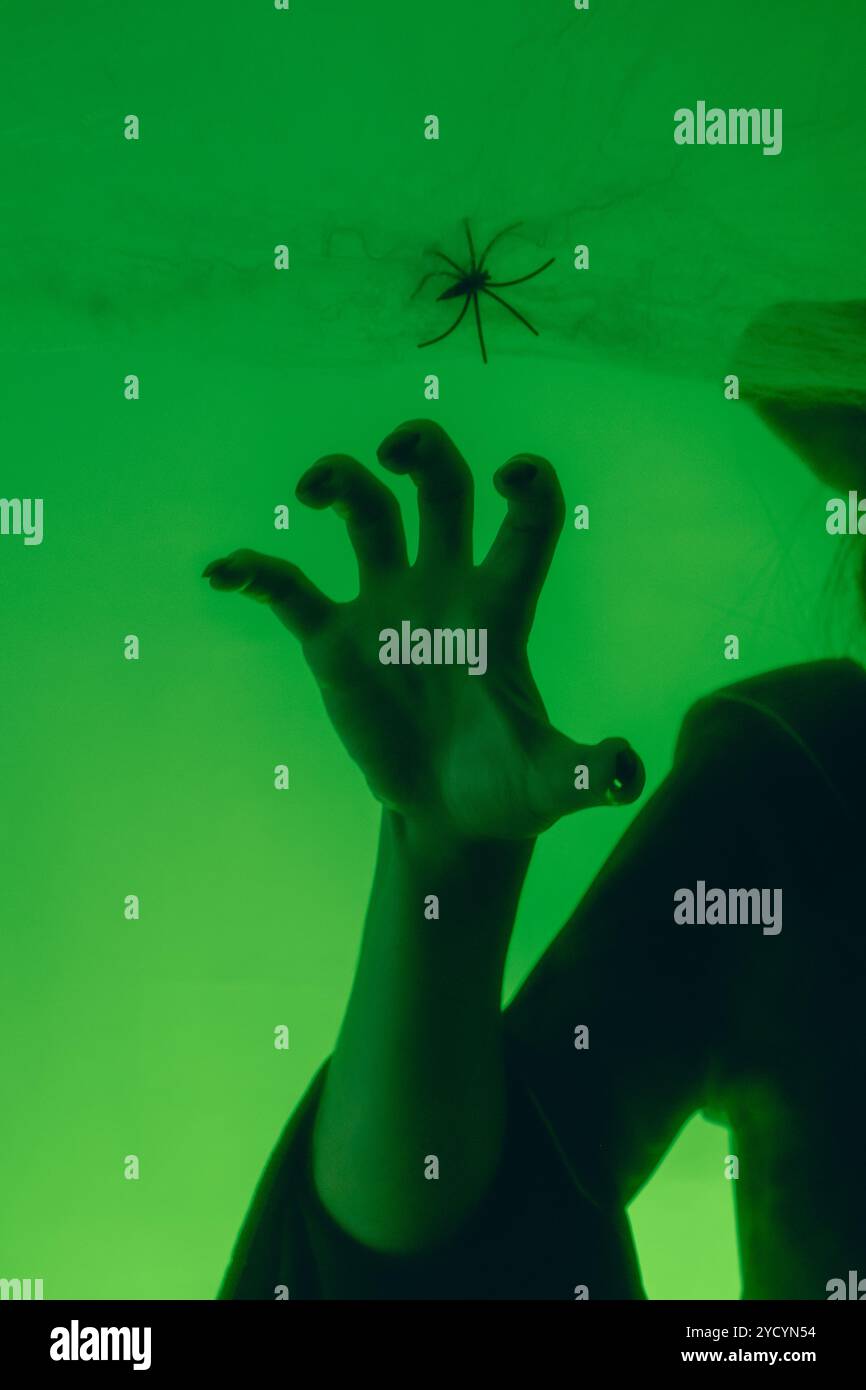 A close-up of a witch's hand silhouetted against a green background ...