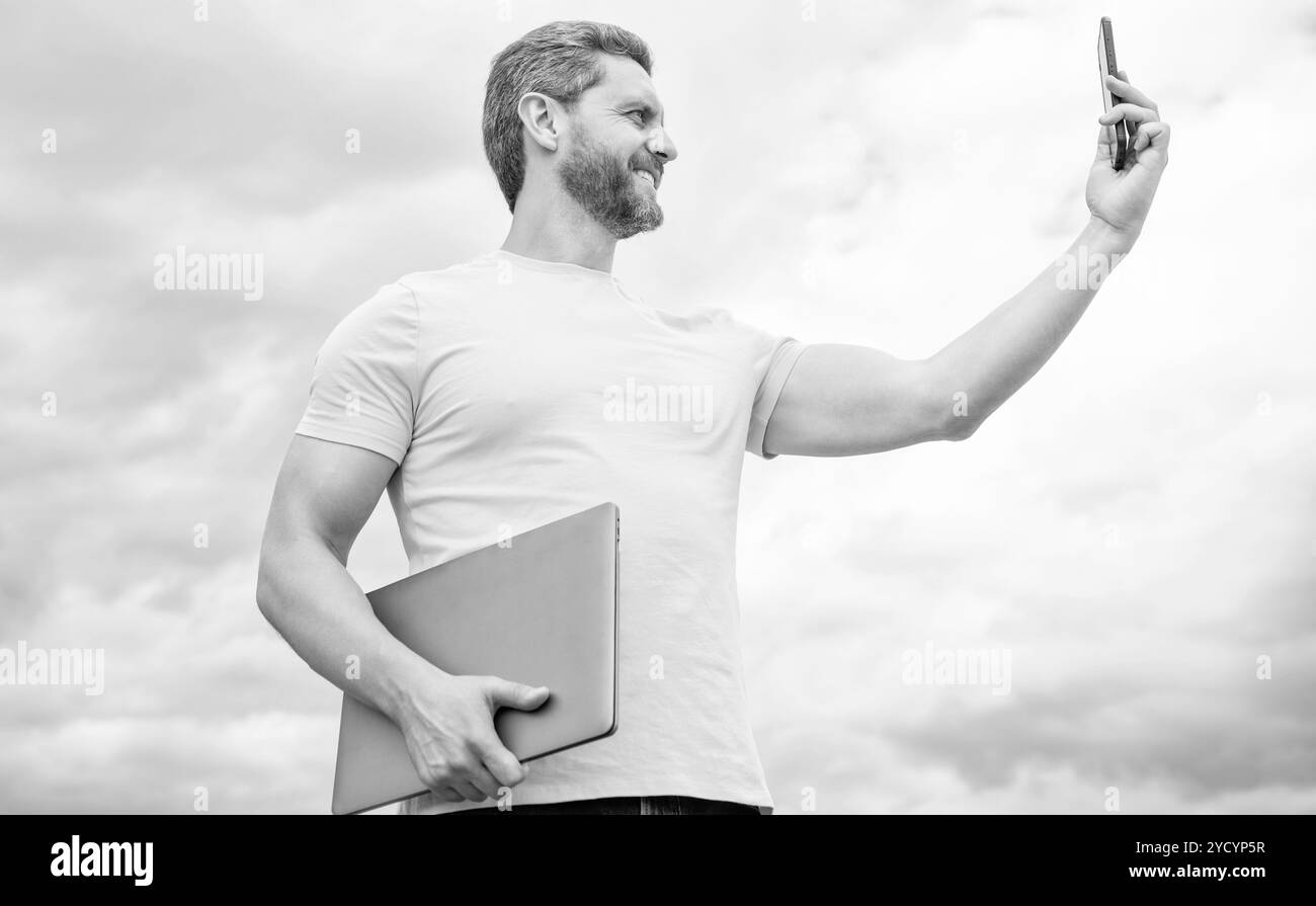 man with laptop making selfie on smartphone on sky background Stock ...