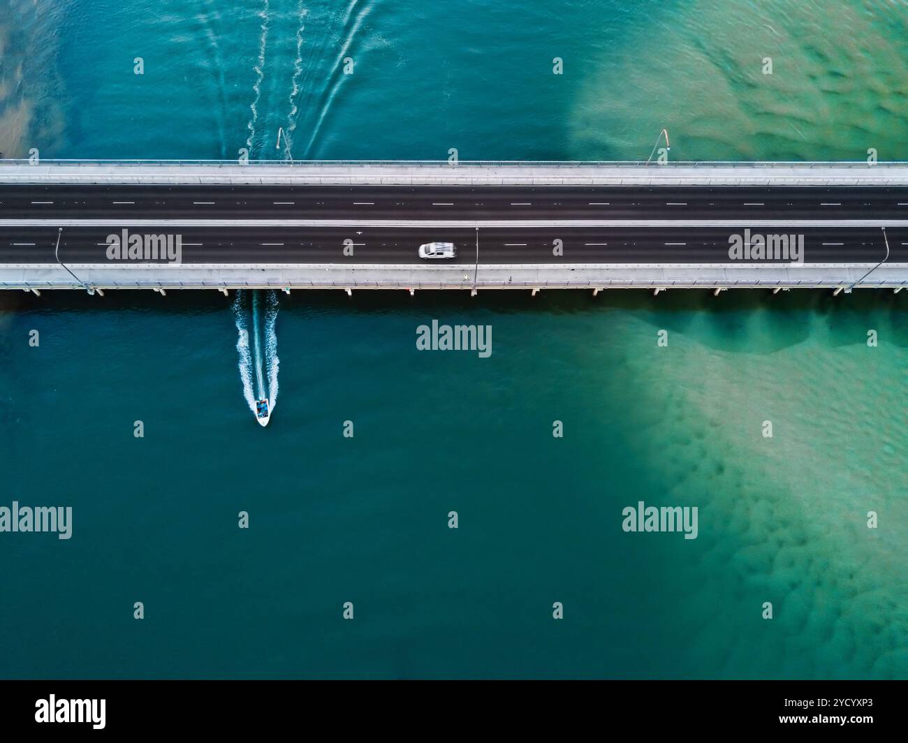A vehicle drives over the bridge as a speed boat travels underneath ...
