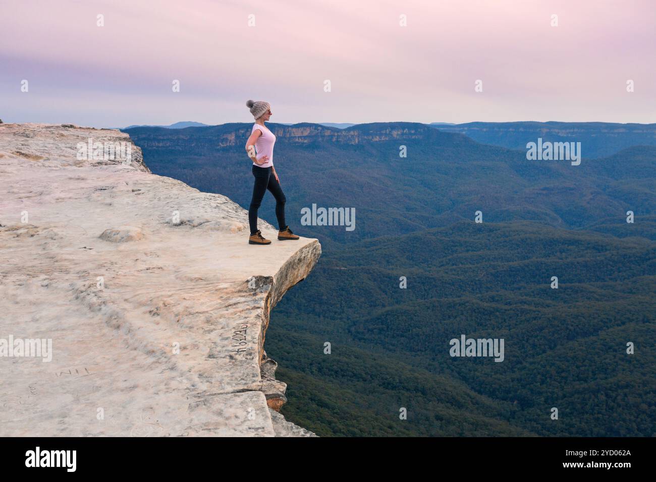Female stands on the escarpment cliff ledge looking out to the valley ...