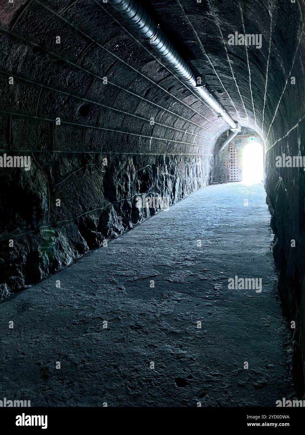A long, dark stone tunnel leading towards light at the end gives off a ...