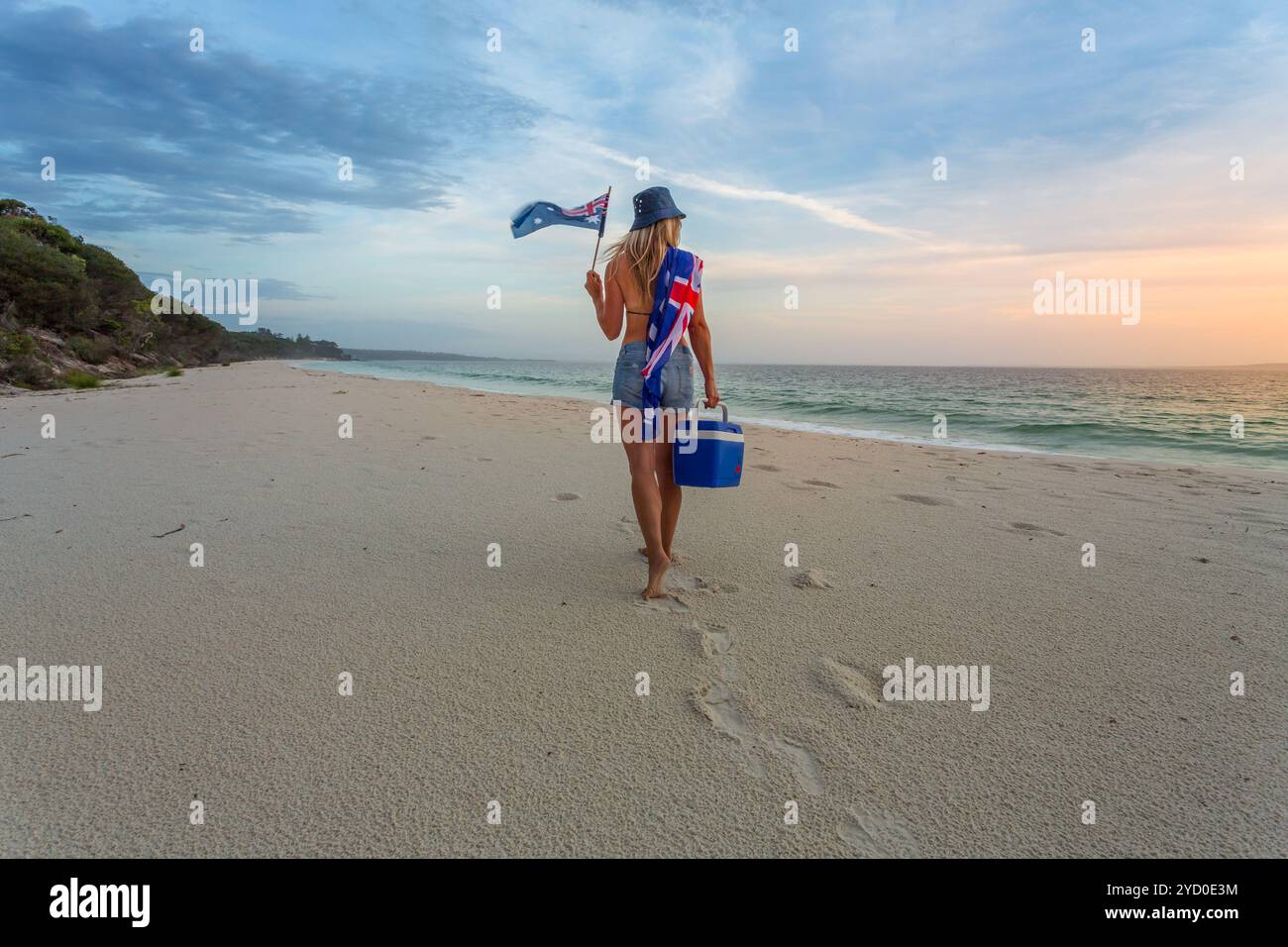 A female walks along the beach at sunrise dressed in shorts and bikini ...