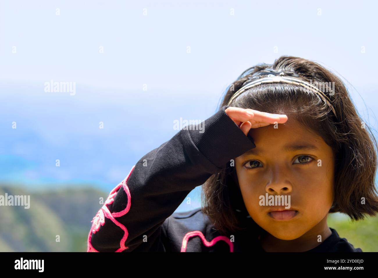 Young girl shielding her eyes from the bright sun with a determined ...