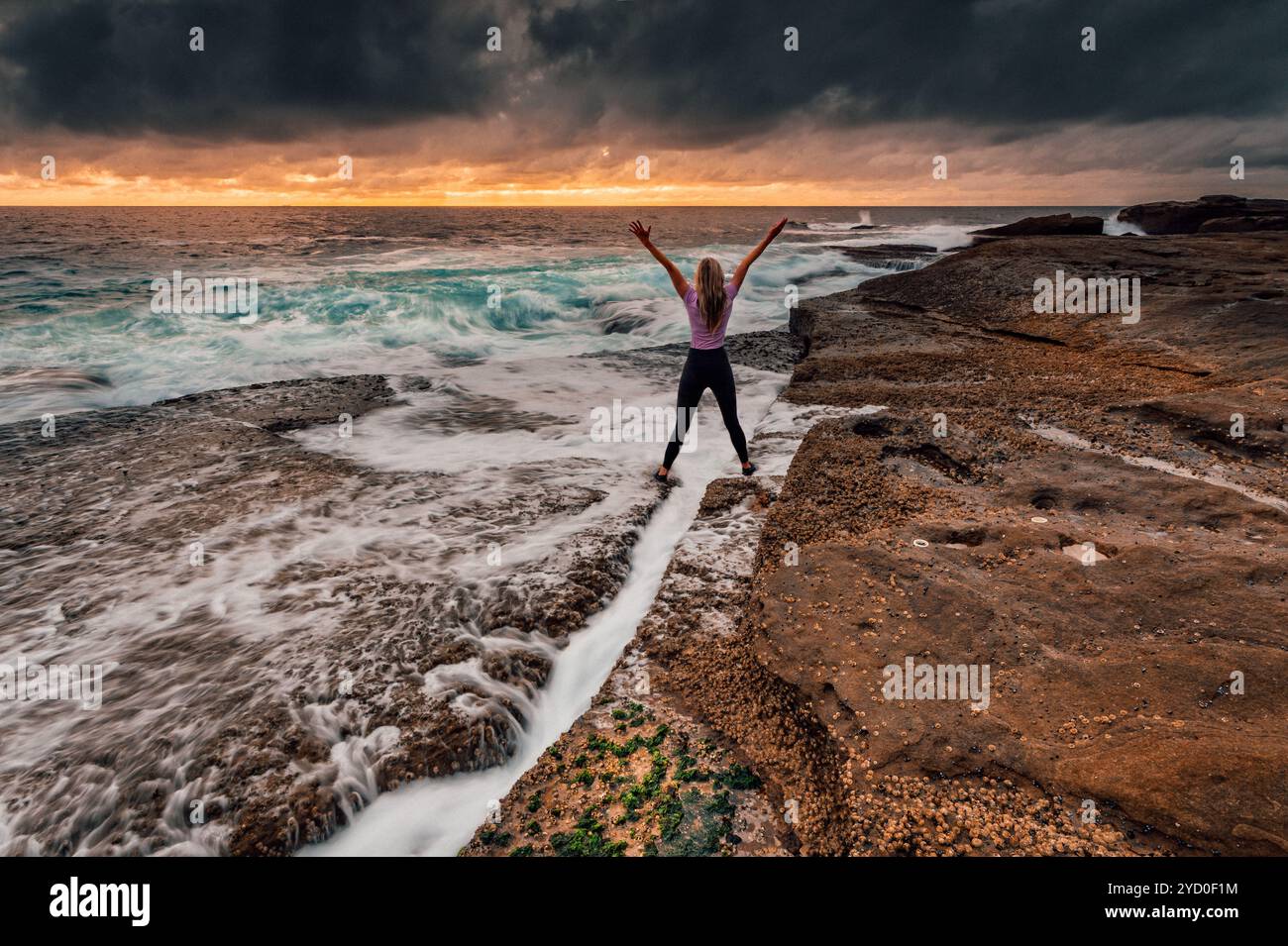 A woman standing over a rock crevice arms outstretched with excitement ...