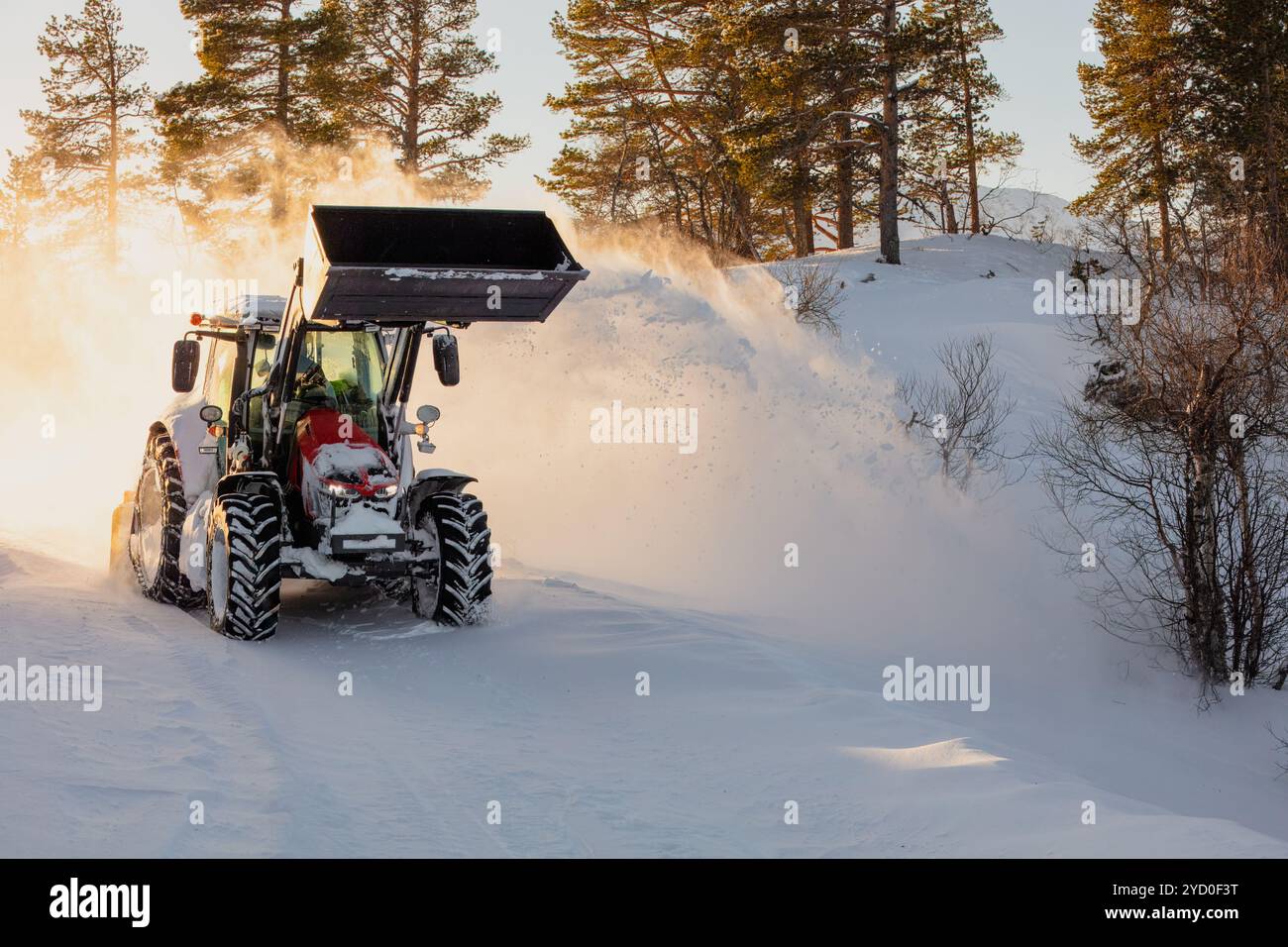 Snow plow tractor cleaning snow with a large bucket on countryside road ...