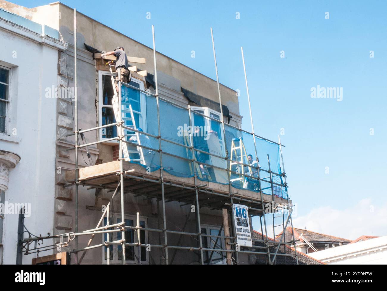 Man working on a ladder replacing timber with scaffolding debris ...