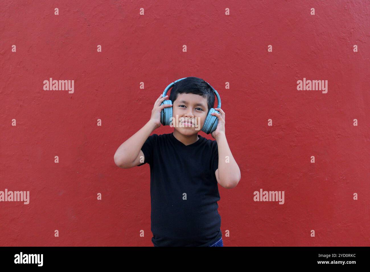 9-year-old dark-skinned Latino boy uses noise-isolating headphones due ...