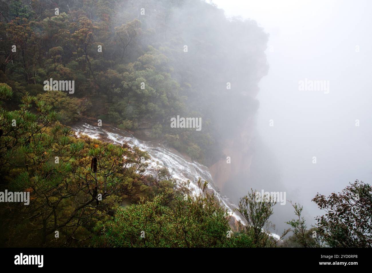 Cloud and mist fill the mountain valley as a waterfall flows off the ...