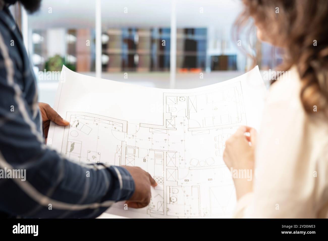 Real estate agent explaining office space layout to client using blueprints and architectural ...