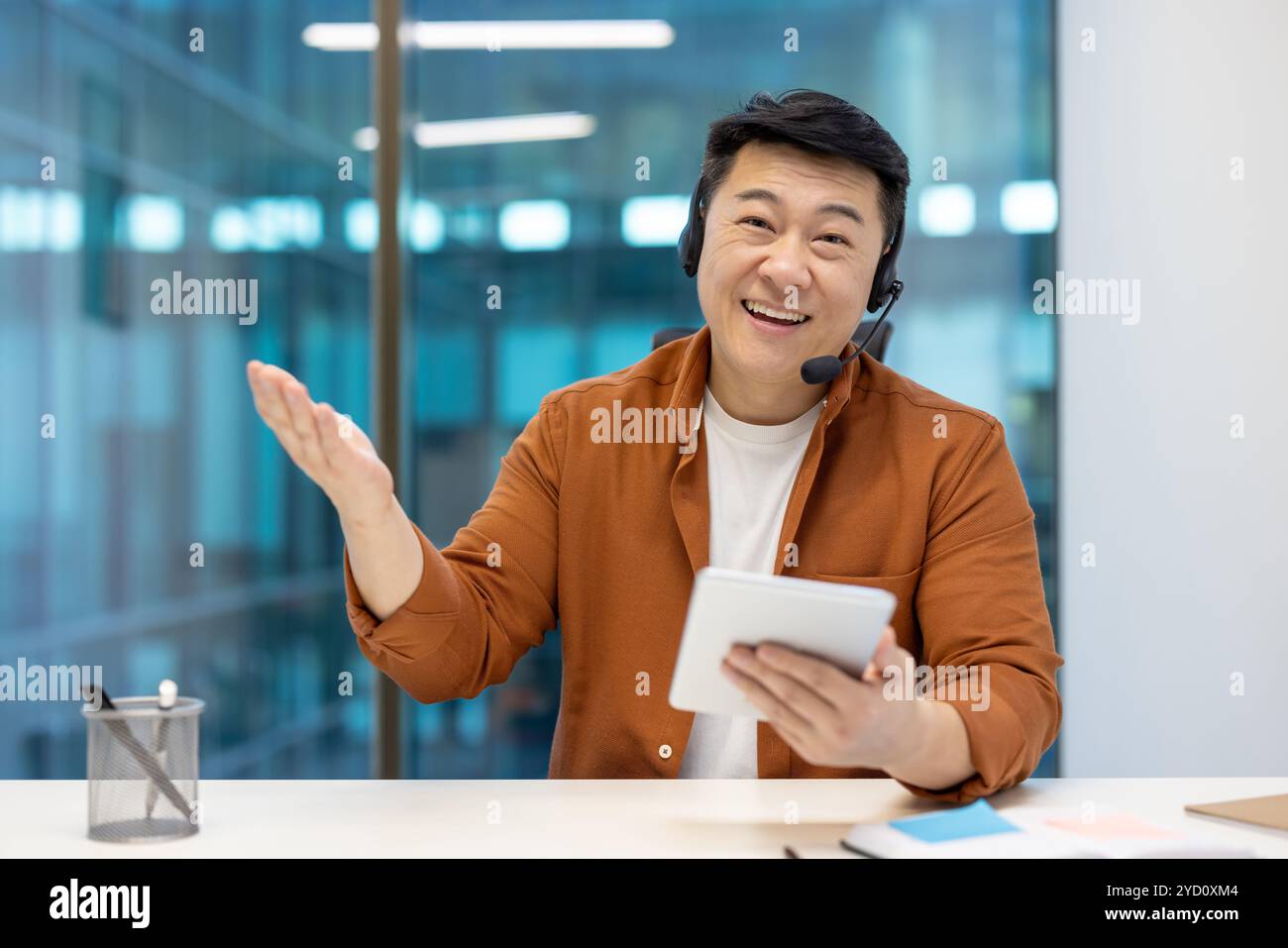 Smiling Asian businessman using tablet and headset for virtual meeting ...