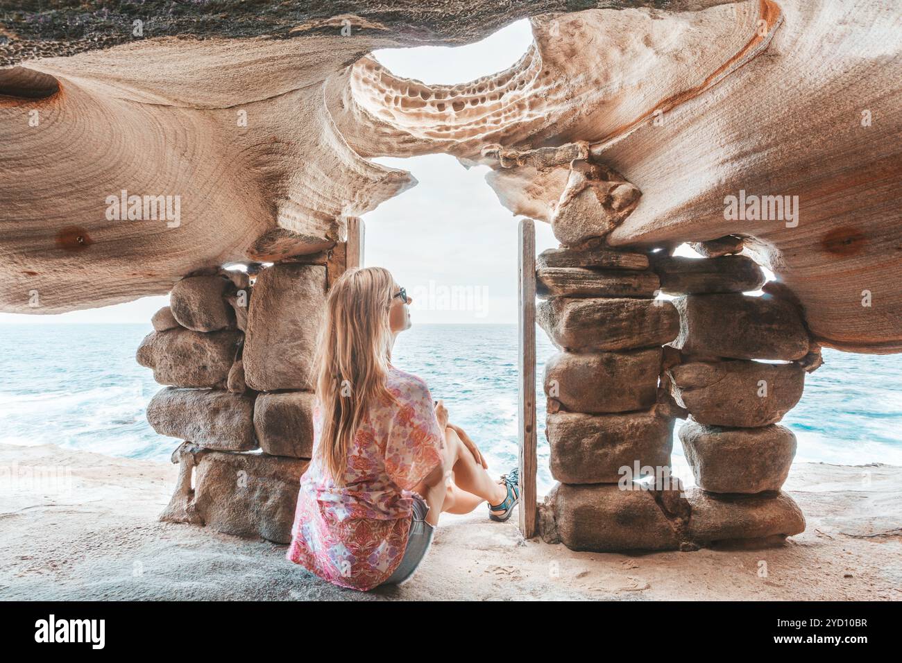 Female sits inside cliff top cave watching the ocean Stock Photo - Alamy