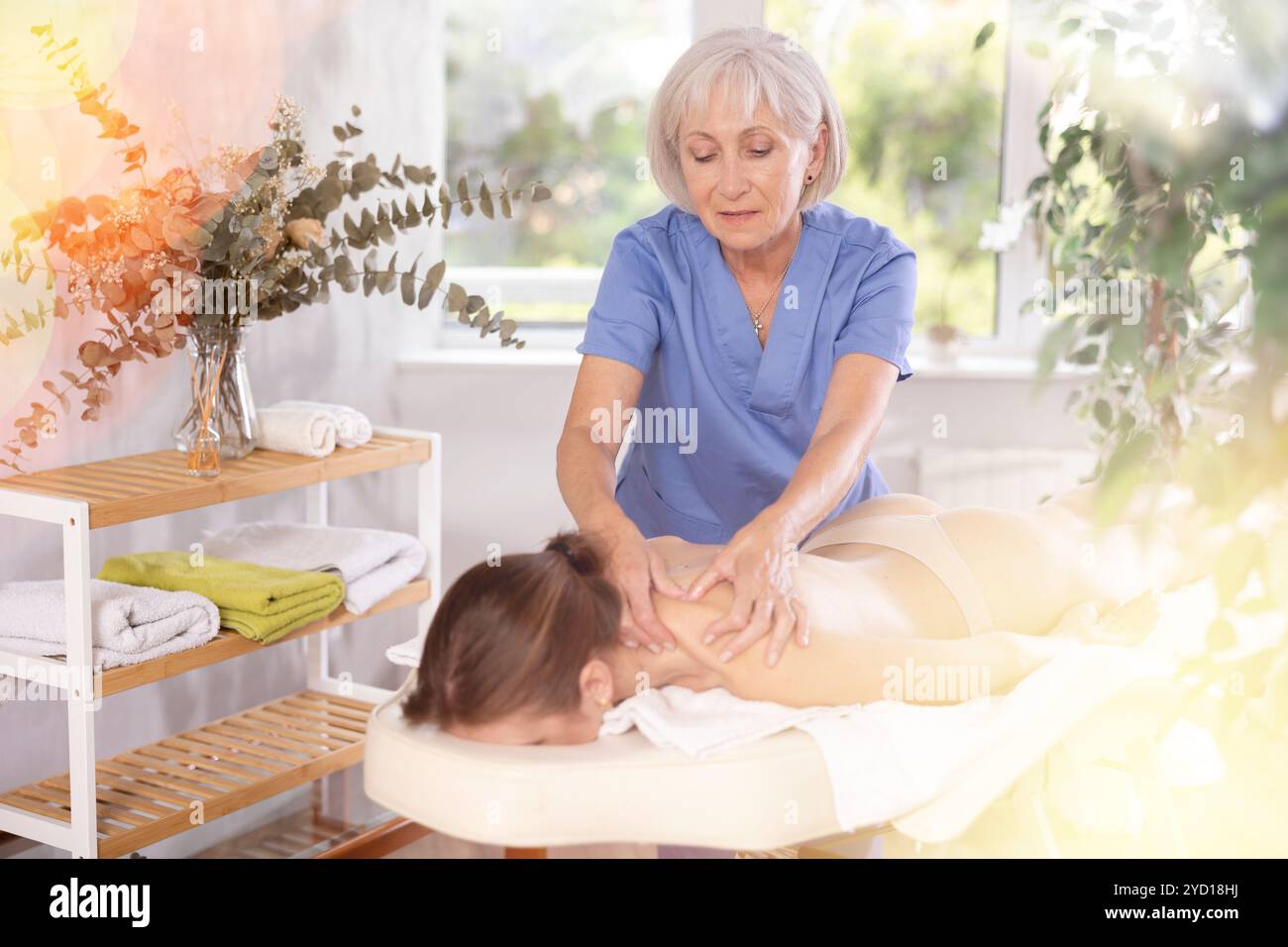 Experienced older professional masseuse doing back massage to young woman Stock Photo - Alamy