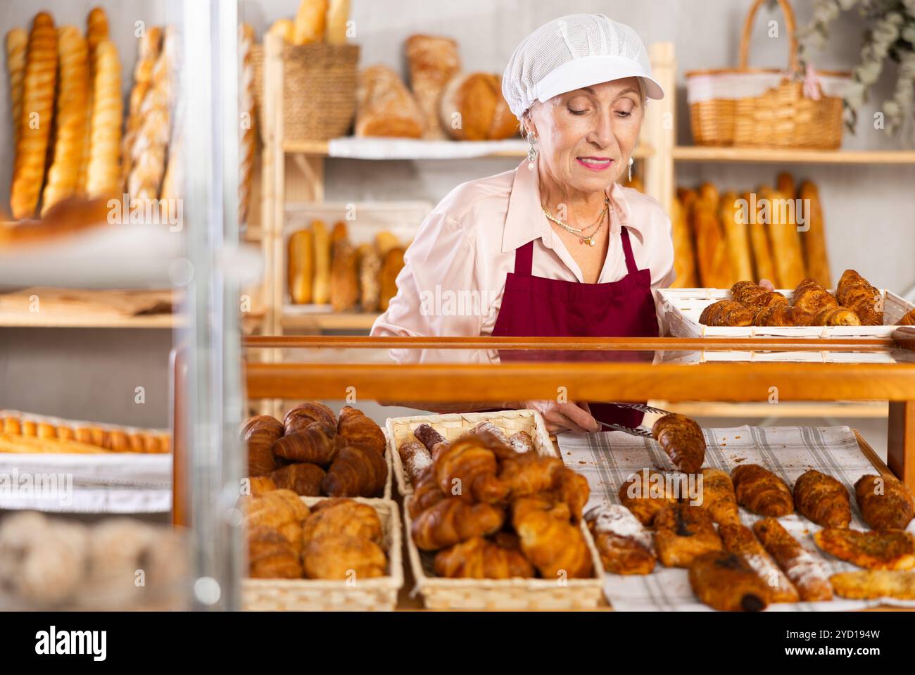 Senior woman employee puts croissants in window, arranges display of ...