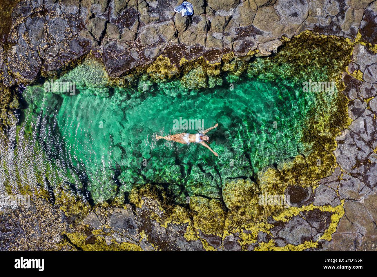 A woman relaxes in a beautiful seaside rock pool with sandy bottom and ...
