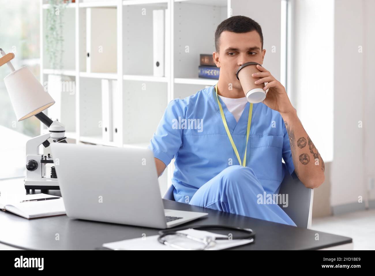 Male doctor drinking coffee at desk in clinic Stock Photo - Alamy