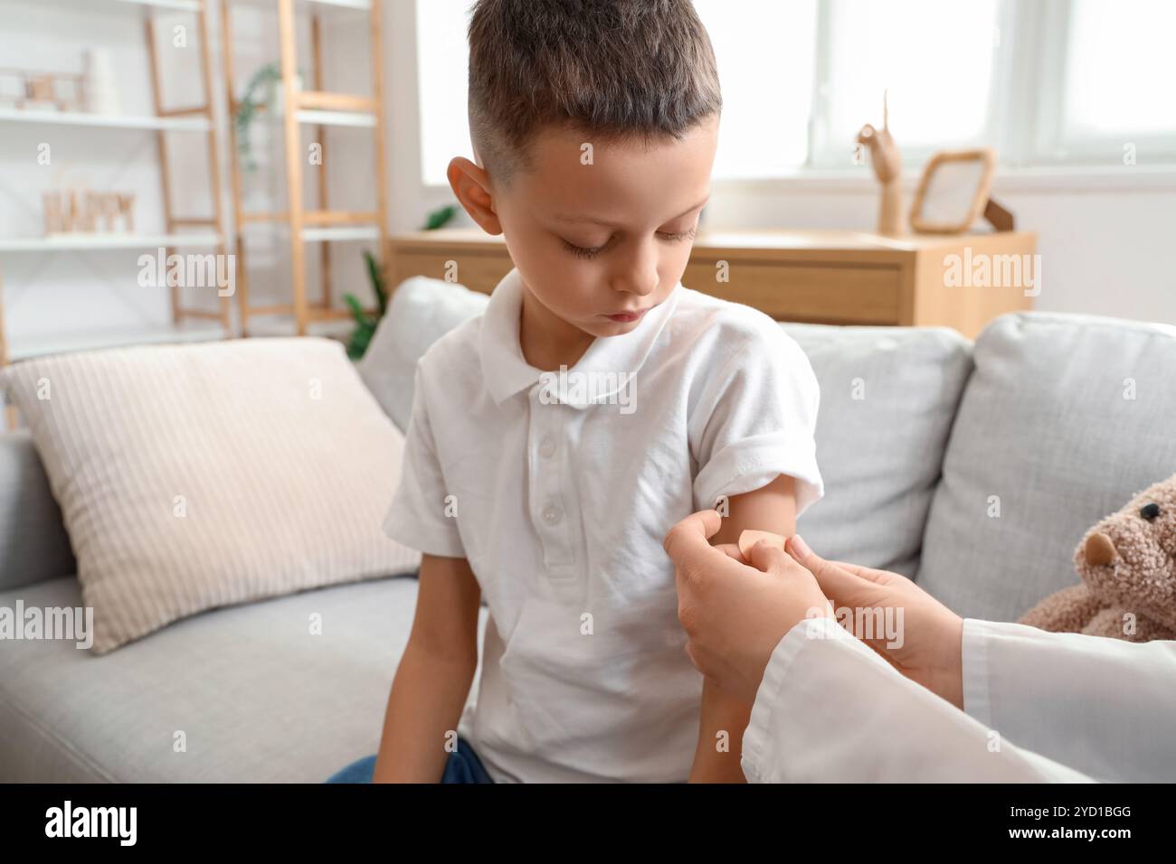 Doctor putting plaster on little boy's arm after vaccination at home ...
