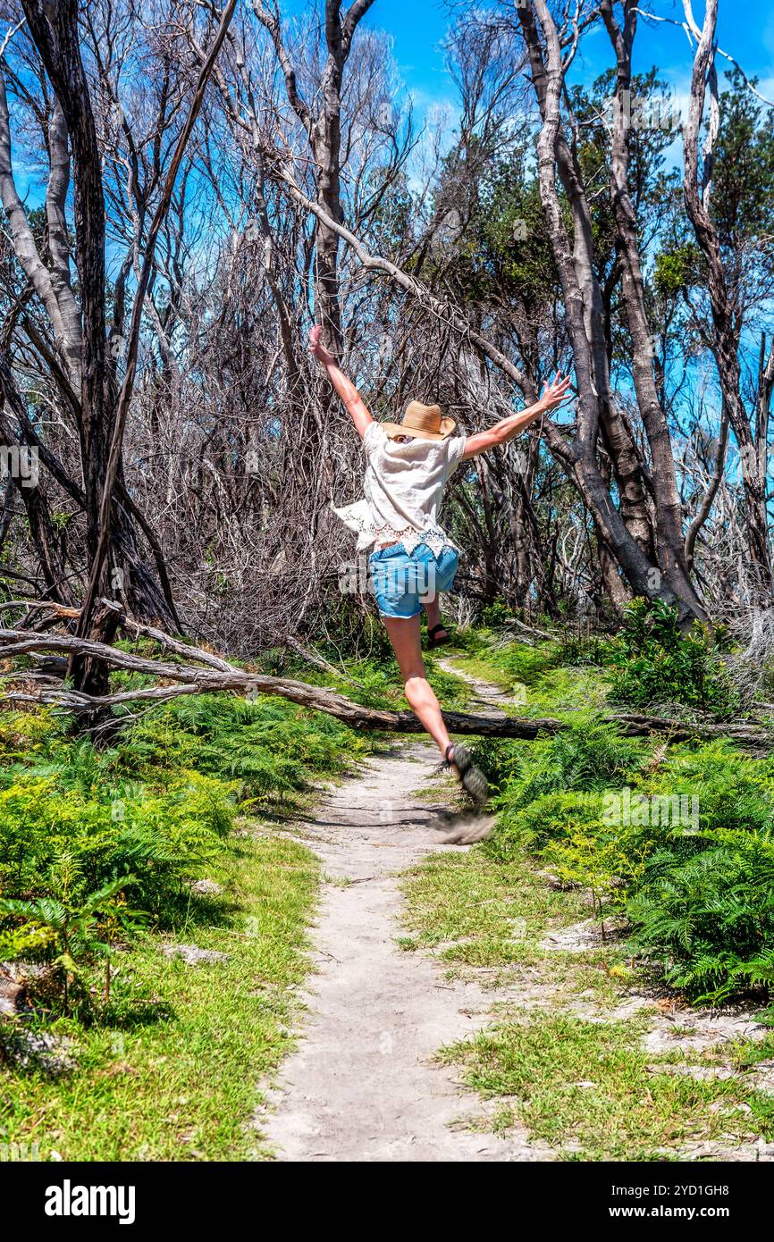 Girl outdoors jumping over tree fallen across track Stock Photo - Alamy