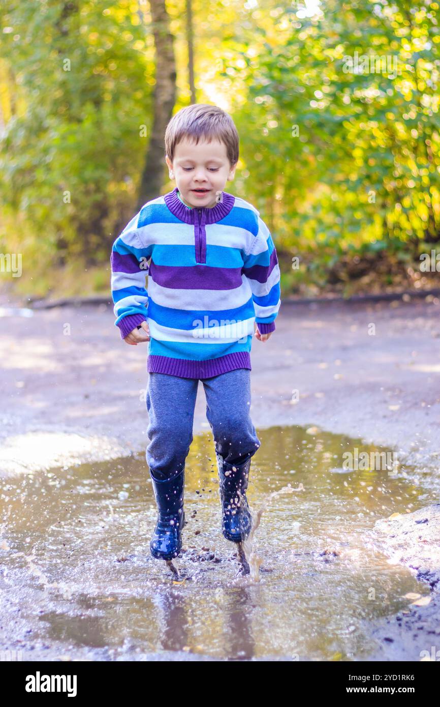 A little boy is jumping in a puddle. A boy in rubber boots. Happy ...