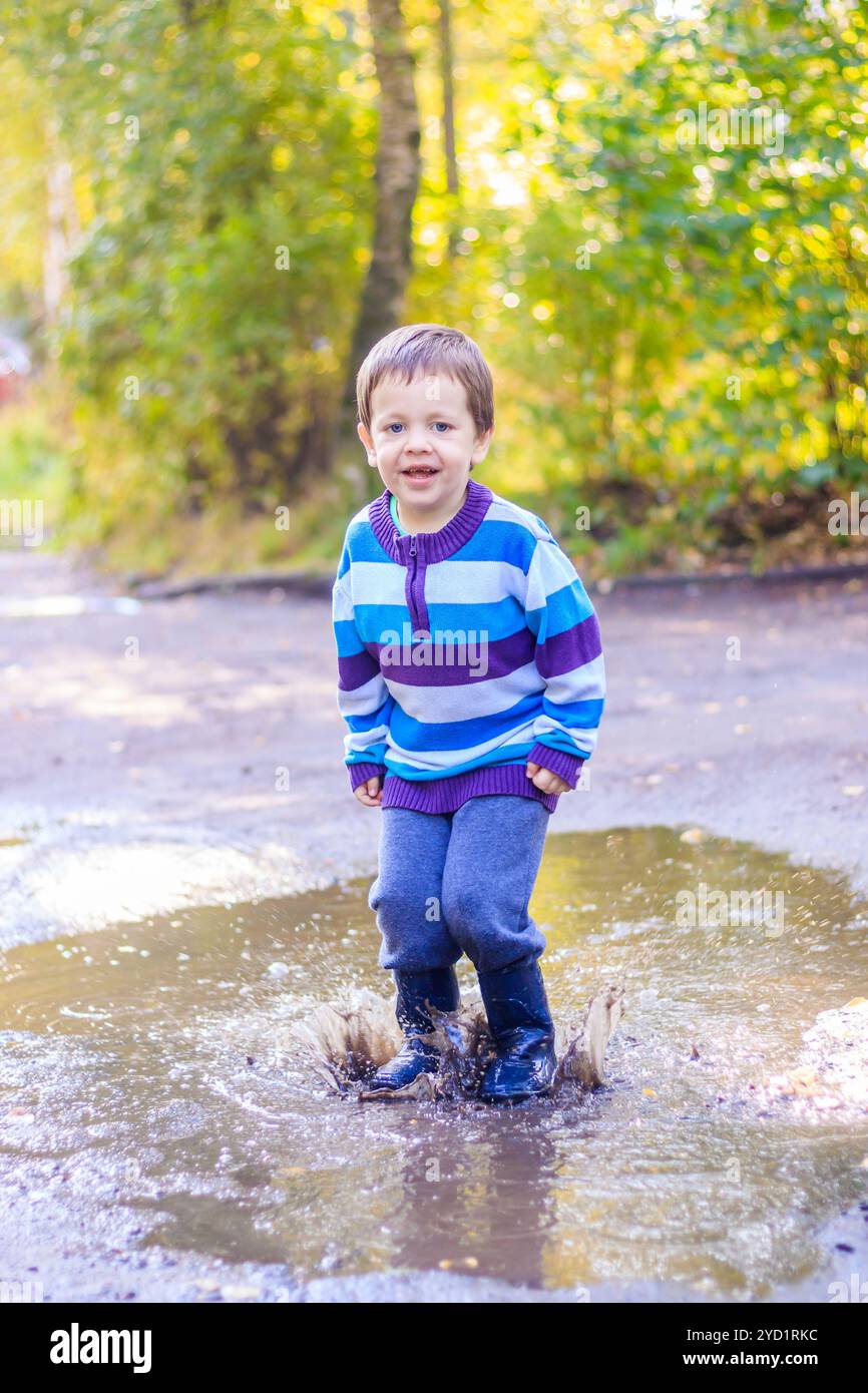A little boy is jumping in a puddle. A boy in rubber boots. Happy ...