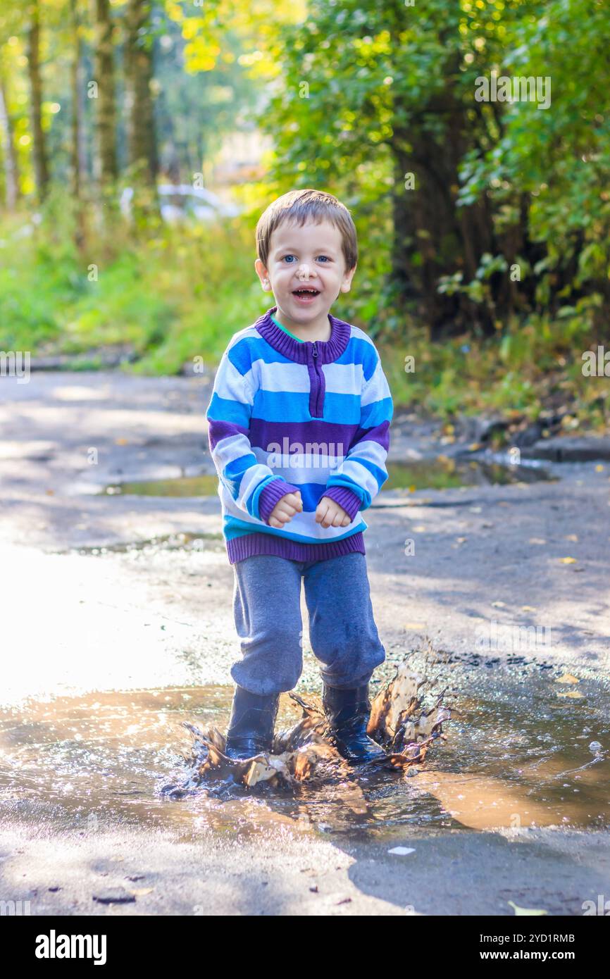 A little boy is jumping in a puddle. A boy in rubber boots. Happy ...