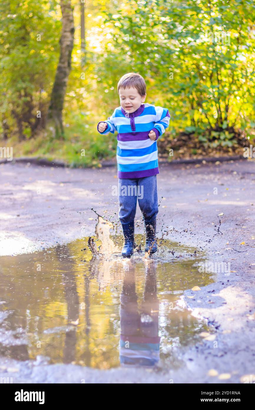 A little boy is jumping in a puddle. A boy in rubber boots. Happy ...